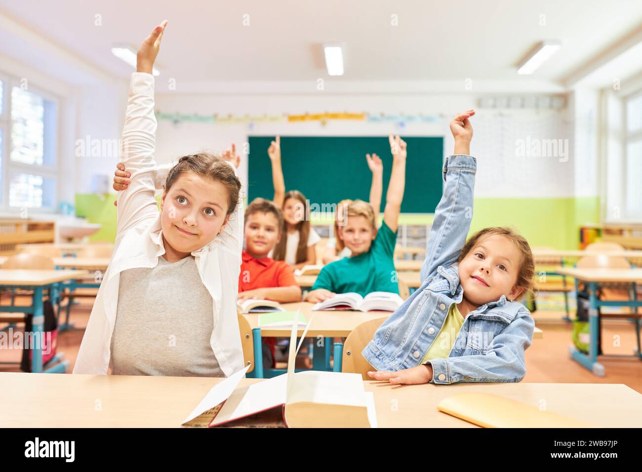 Classmates raising hands while sitting on bench during lecture in class ...