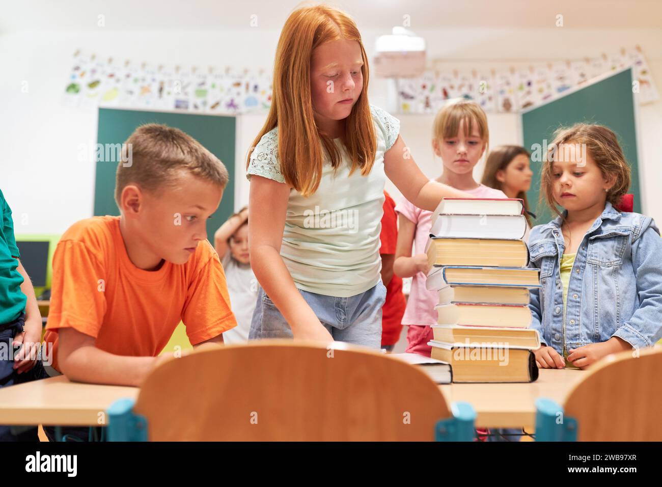 Girl stacking books on bench with classmates during activity in ...