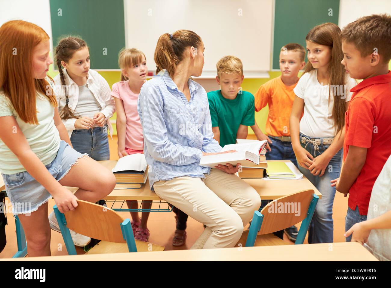 Female teacher reading book to elementary school children in classroom ...