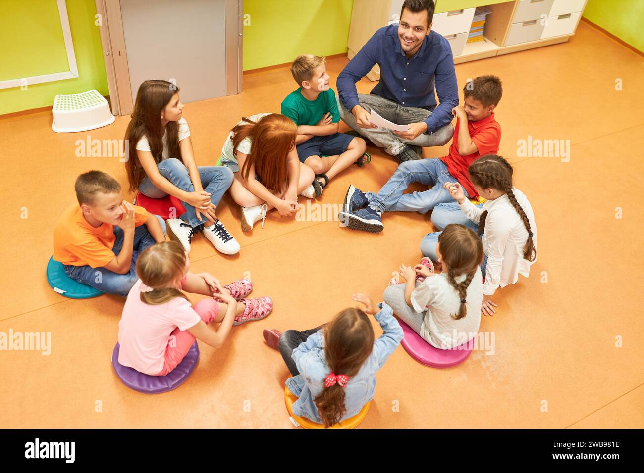 High angle portrait of smiling male teacher sitting in circle with ...