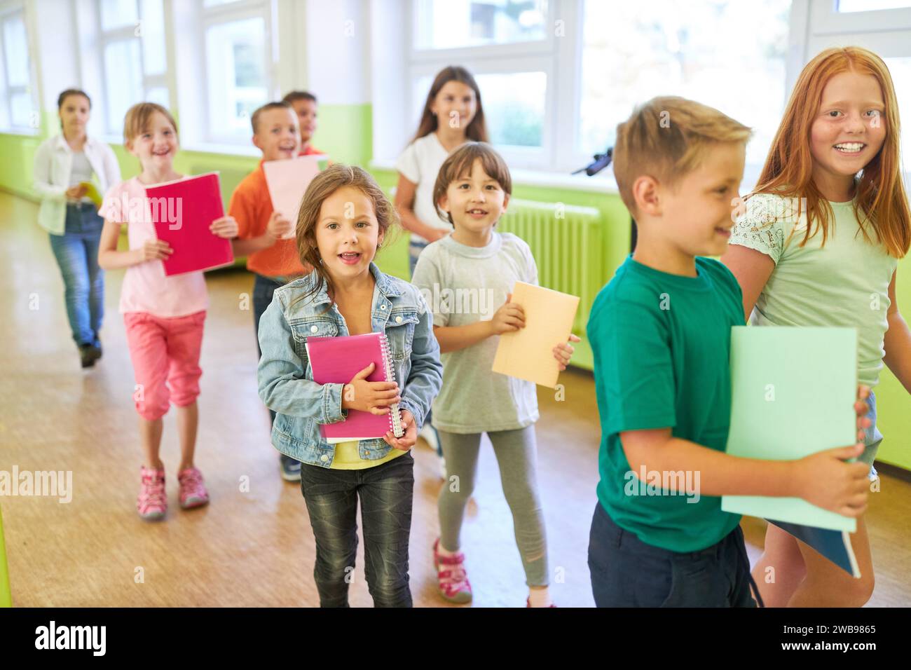 Schoolkids holding books while walking together in hallway during ...