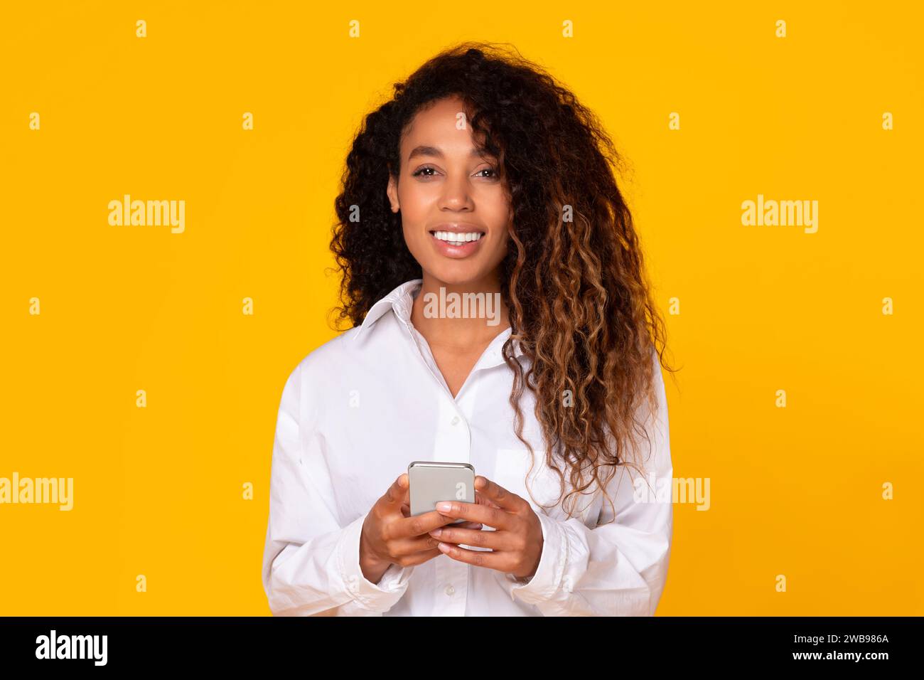 Portrait of black young lady scrolling on smartphone, yellow background ...