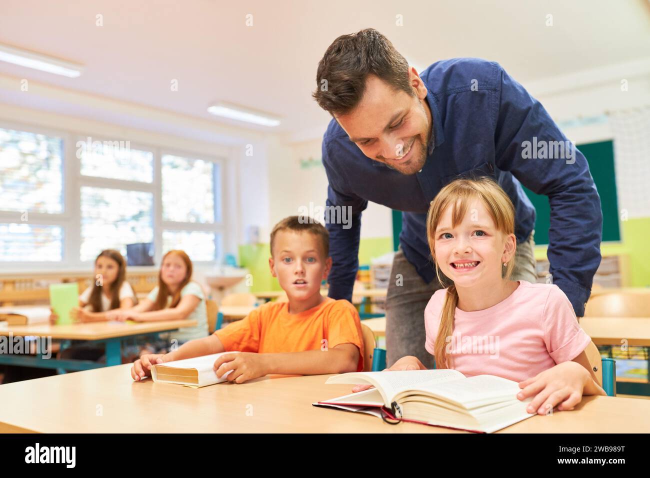Happy male teacher standing near students reading books while sitting ...