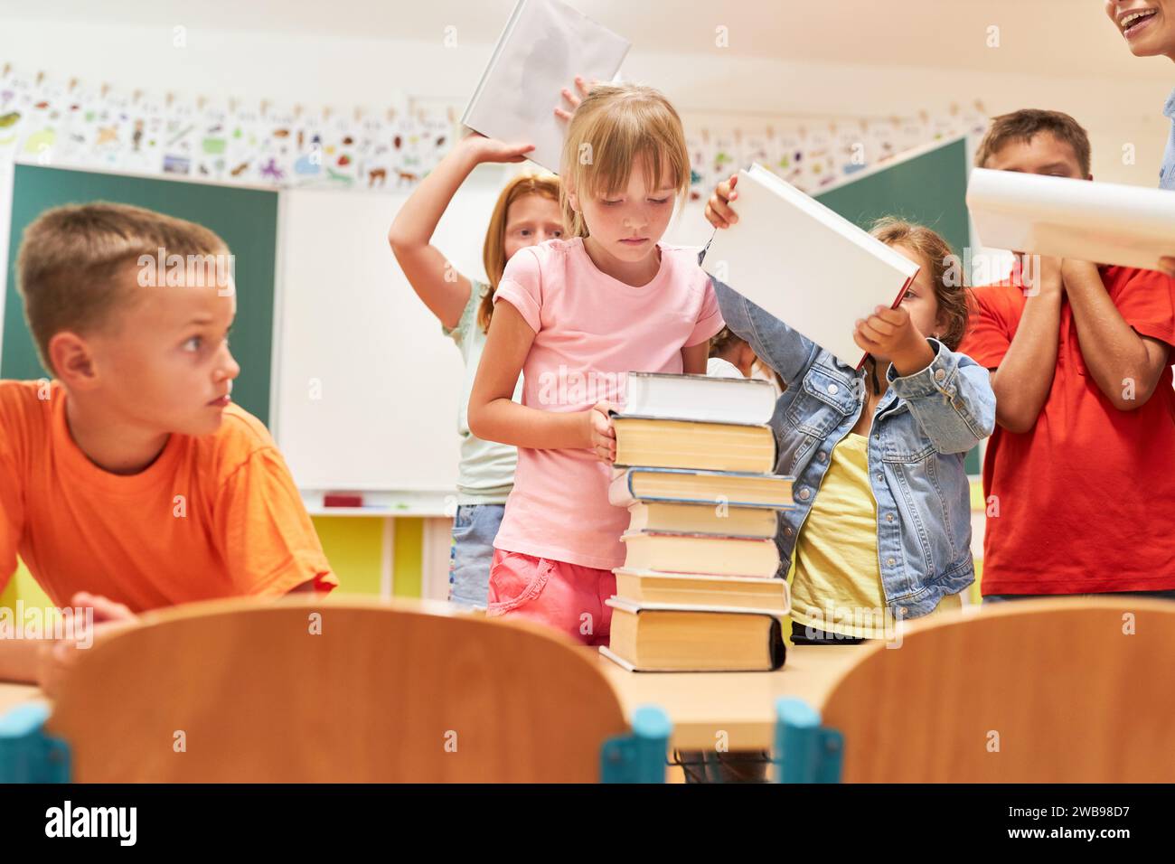 Classmates stacking books on bench during activity in classroom Stock ...