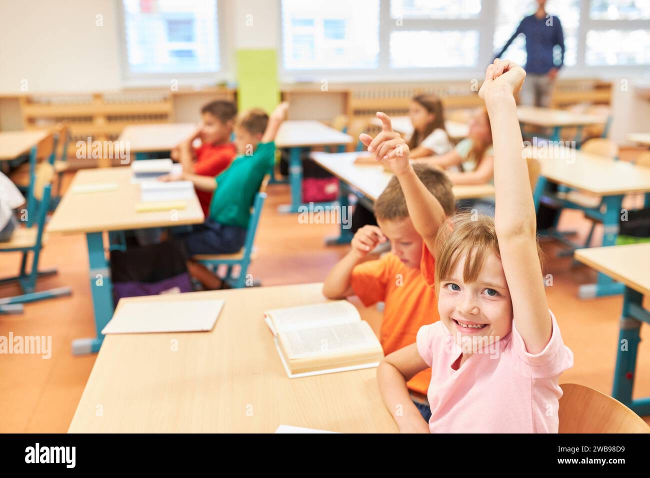 Smiling schoolgirl raising hand while sitting with male friend during ...