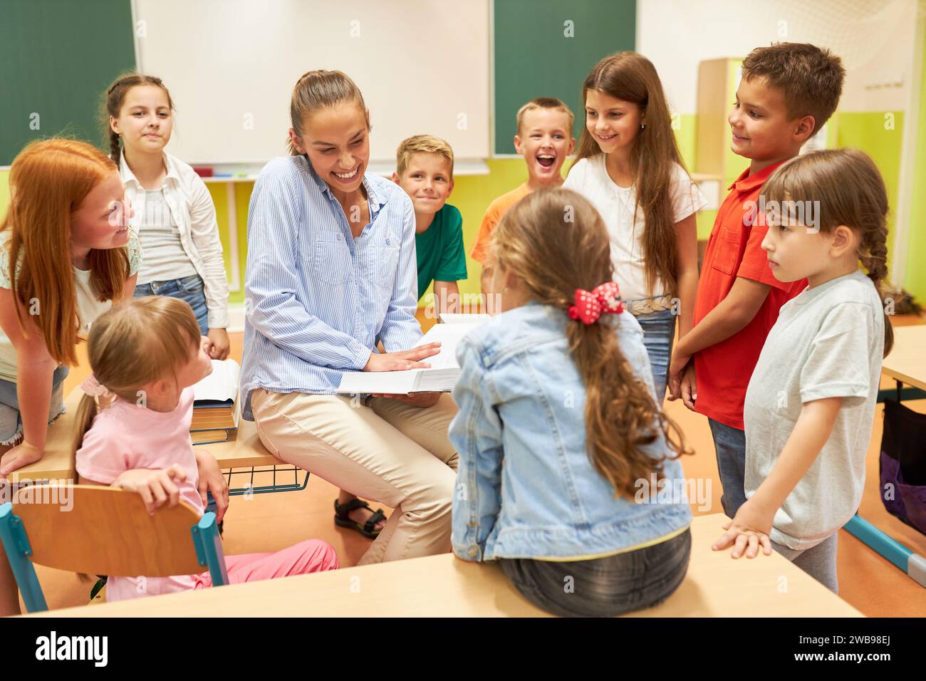 Happy female teacher holding book while sitting on bench with students ...