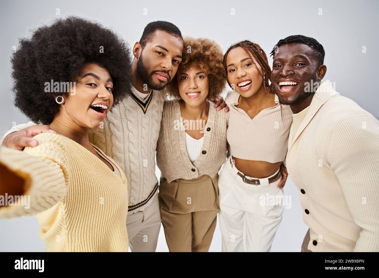 group of smiling african american friends bonding and hugging on grey ...