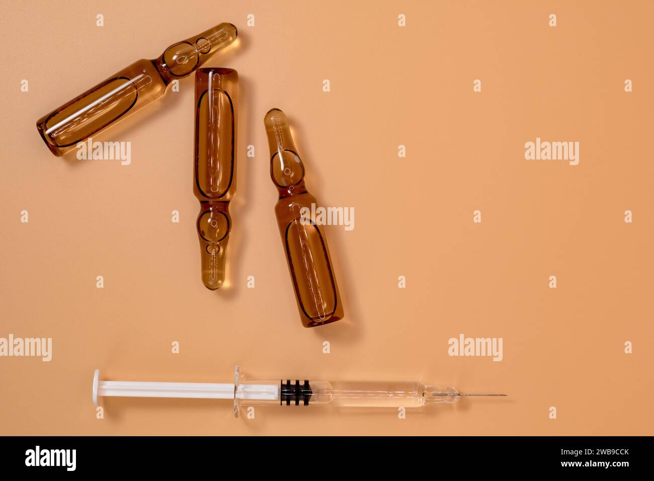 Small full syringe with needle on peach background. Next to it is the ...