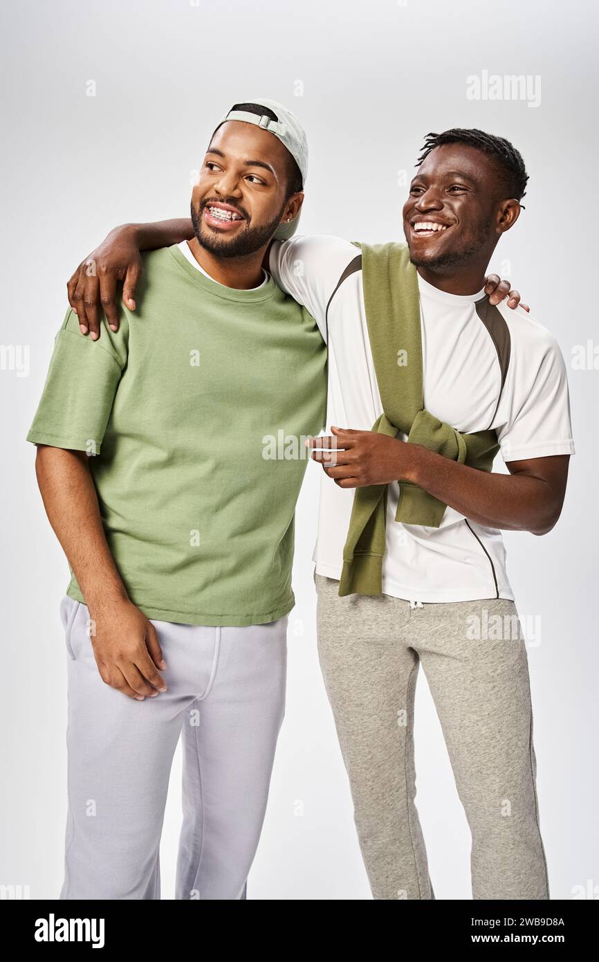 positive african american male friends in casual wear hugging on grey ...