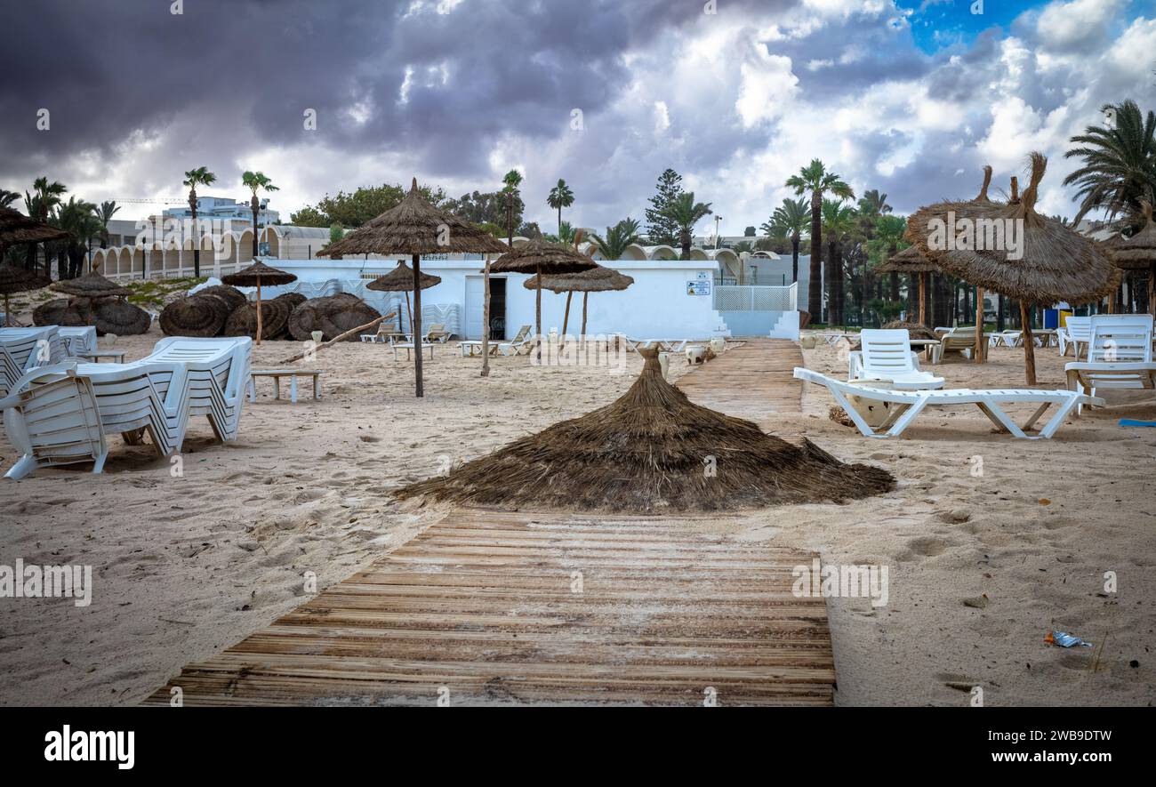 A broken thatched parasol and plastic sun loungers on a delapidated ...