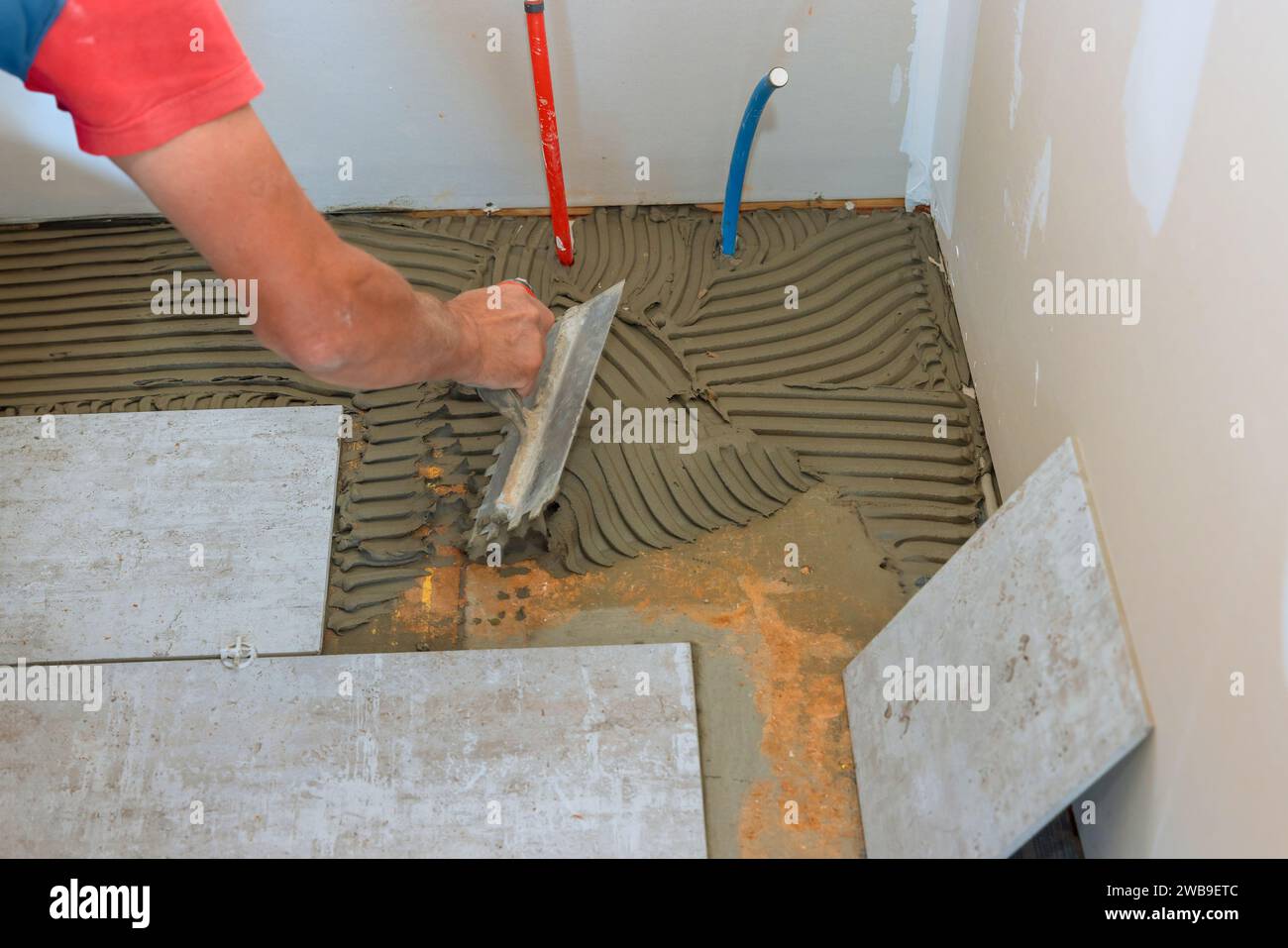 Preparing concrete floor for tiling by troweling adhesive onto surface ...
