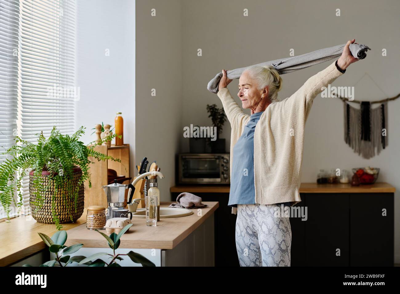 Active senior woman in sportswear holding towel over head between ...