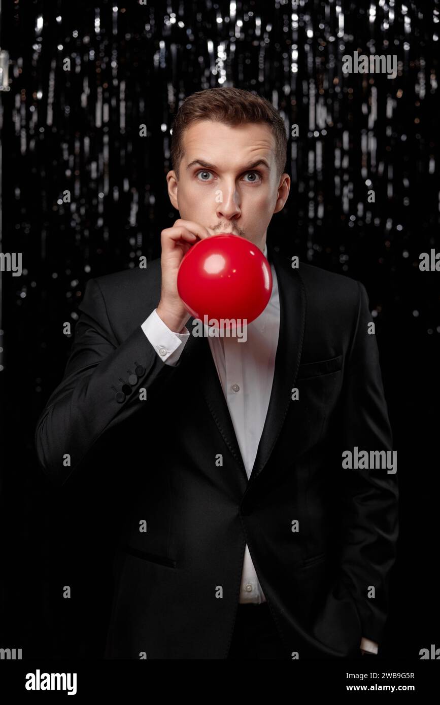 caucasian man in black jacket blowing red air balloon on glitter ...