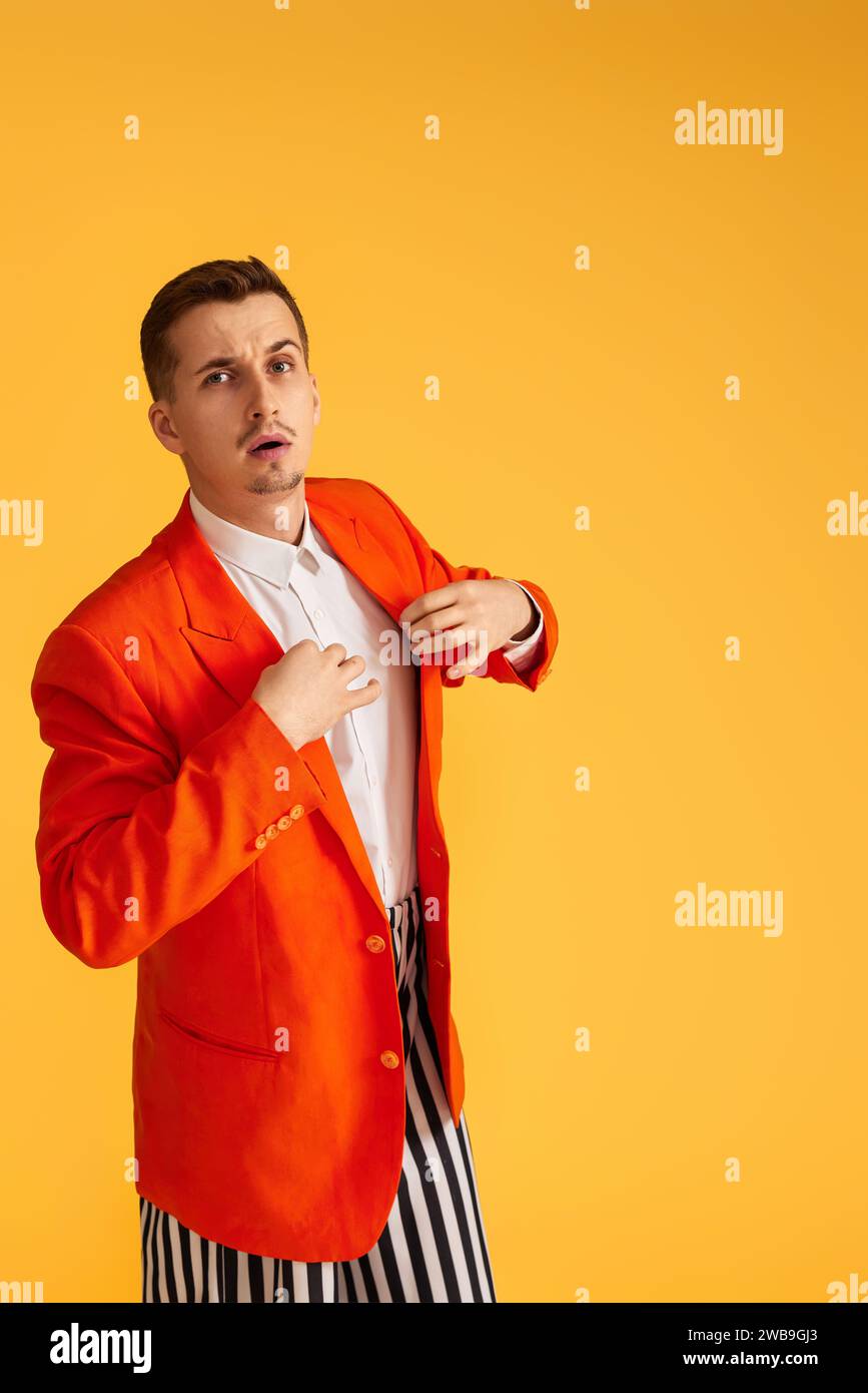 extravagant young man in orange jacket and striped pants on yellow ...