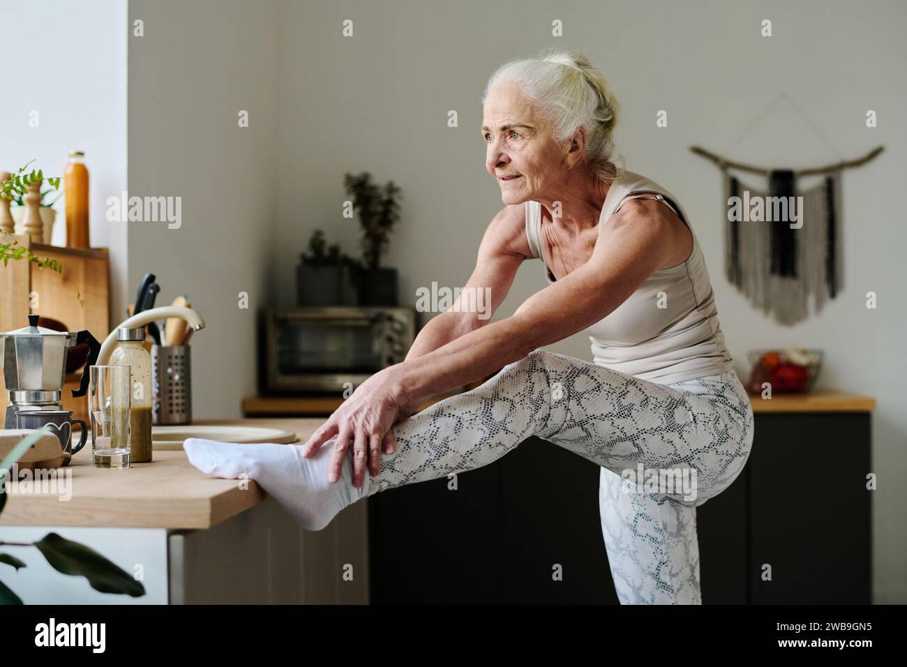Active senior woman making effort while stretching arms over raised leg ...