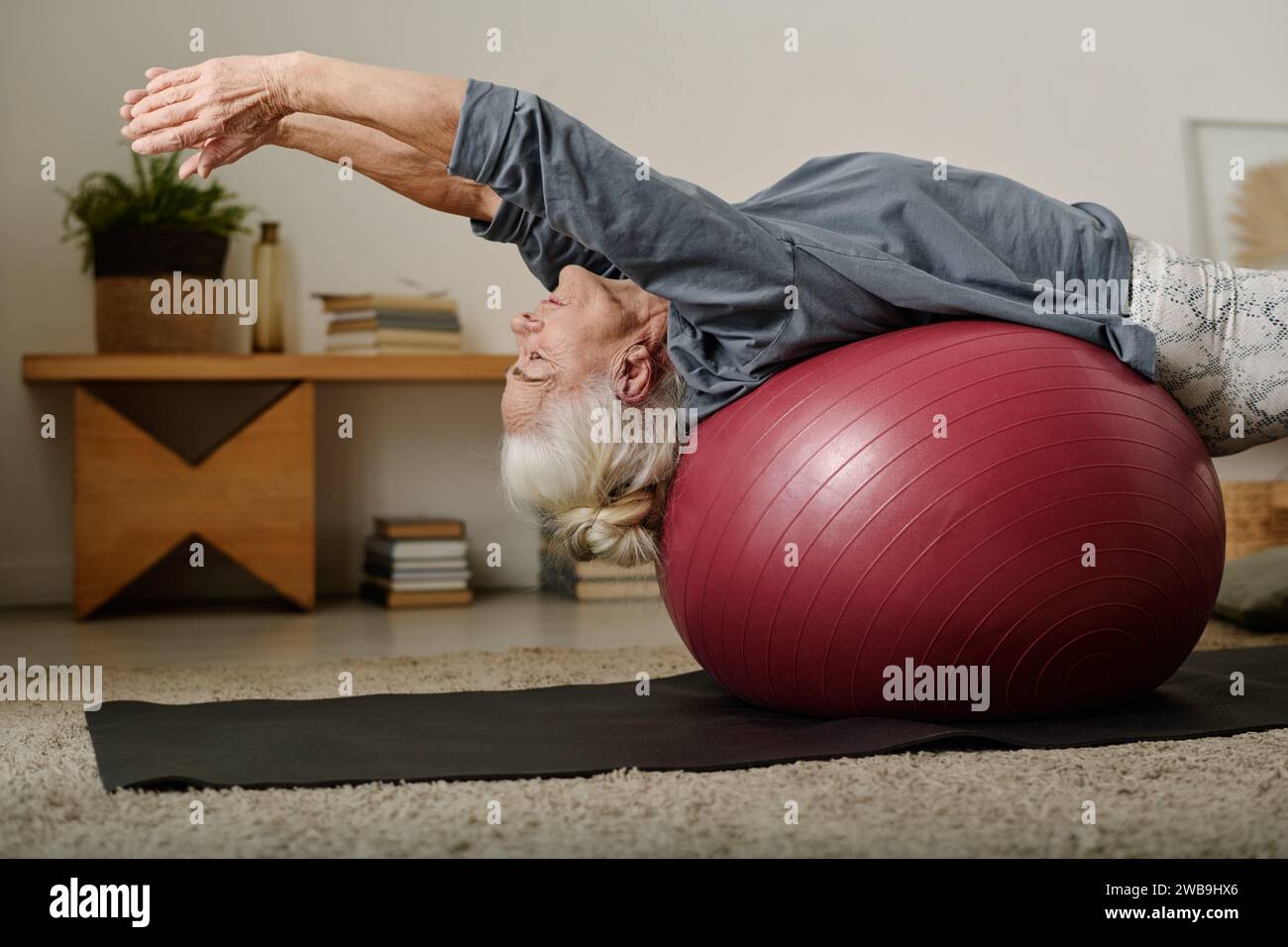 Side view of grey haired woman in activewear lying on fitball and ...