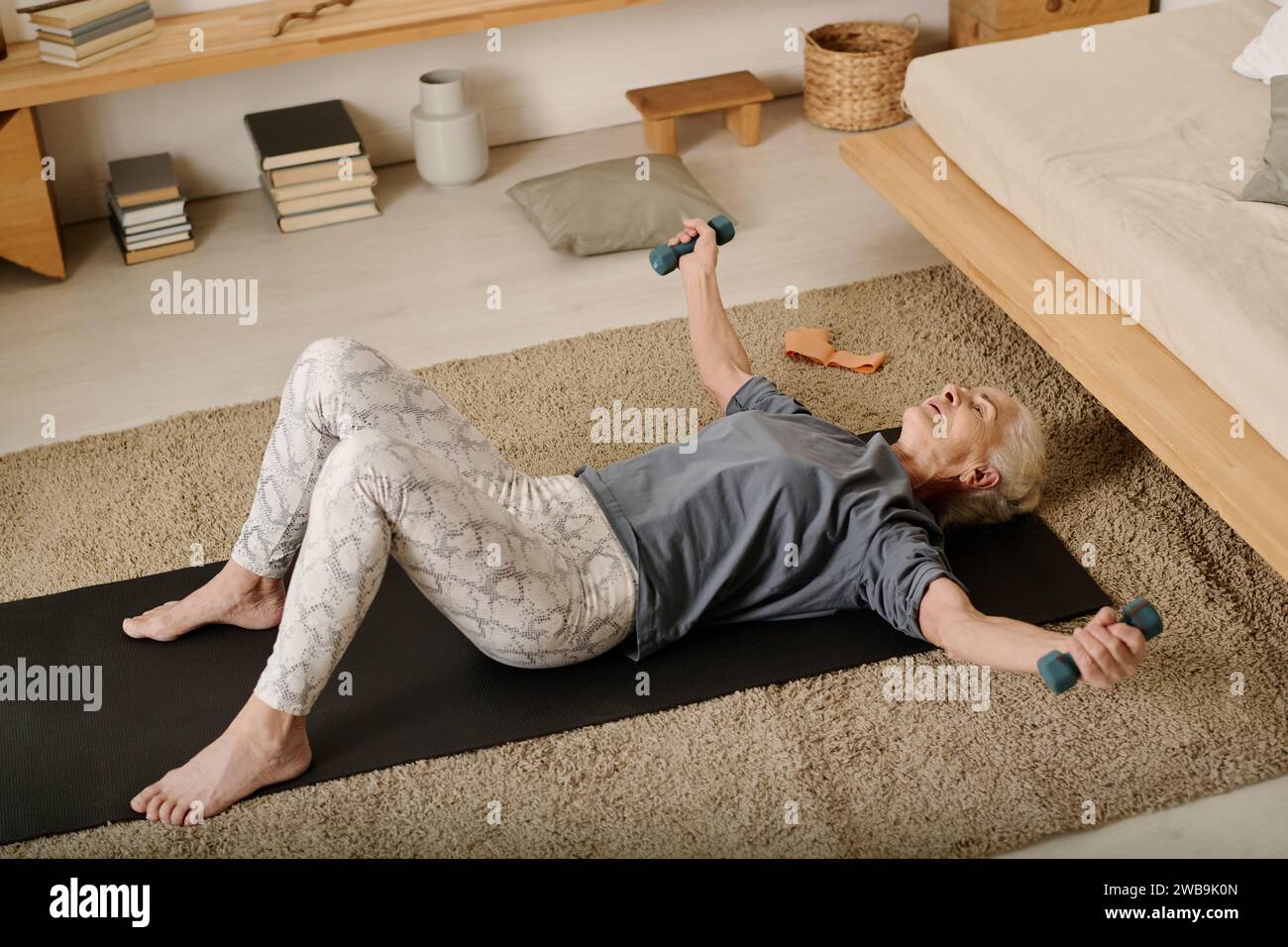 High angle of aged woman in activewear lying on mat in bedroom and ...