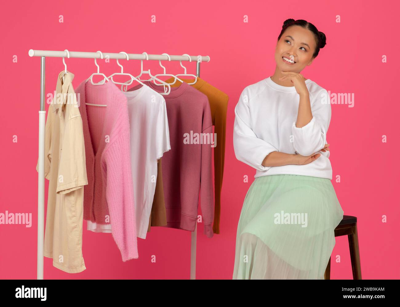 Pensive Asian Woman Sitting On Chair Near Clothing Rack Stock Photo - Alamy