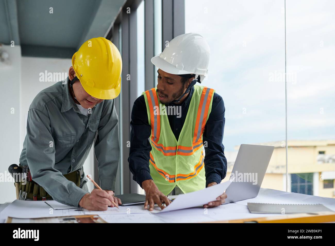 Construction worker double checking measurements in building blueprints ...