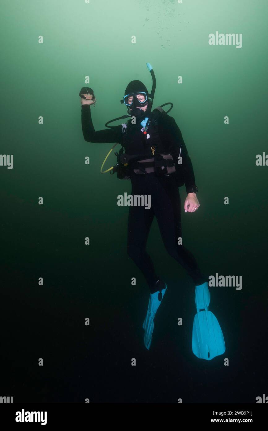 A female scuba diver holding the reel of a surface marker buoy at a ...