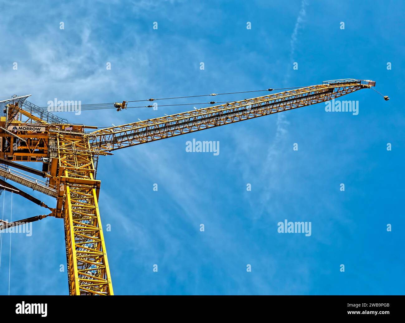 A bright yellow Morrow luffing jib tower crane stands idle, attached to ...