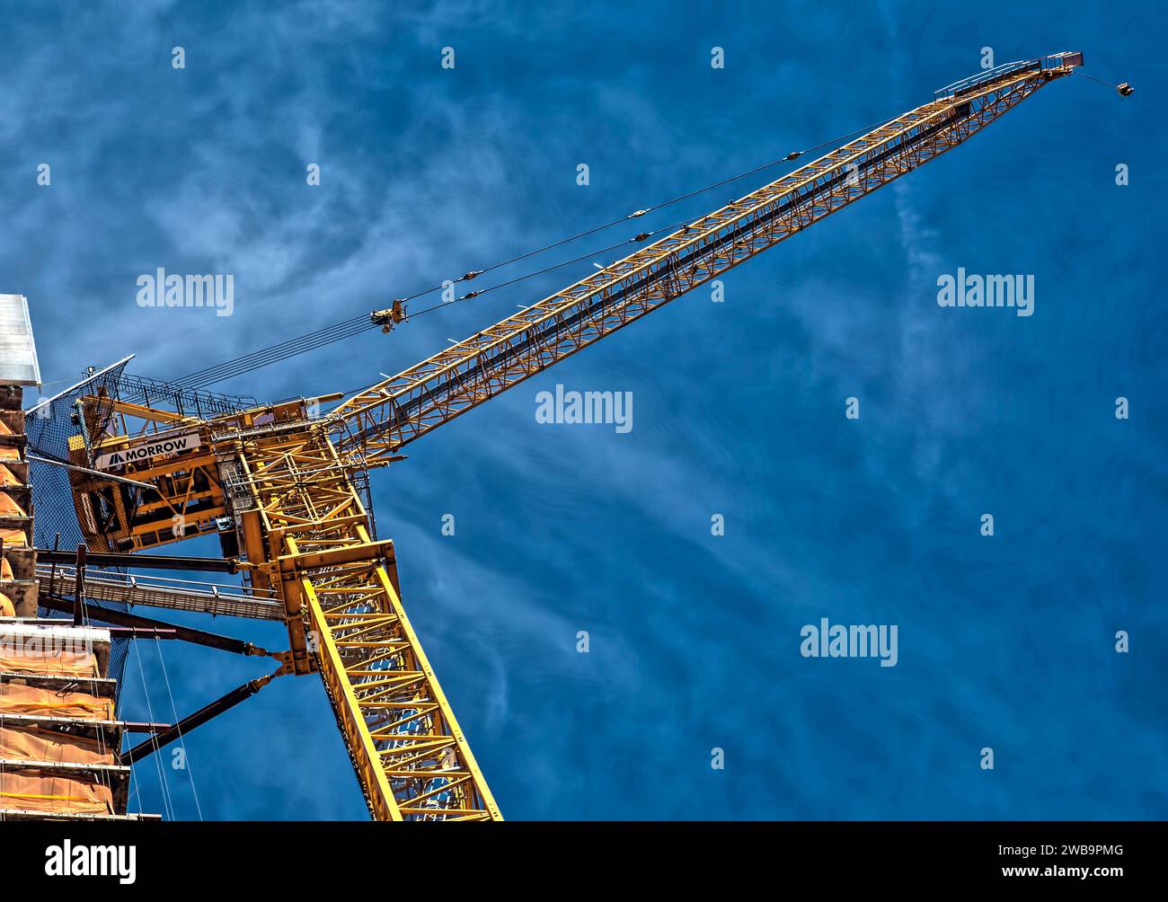 A bright yellow Morrow luffing jib tower crane stands idle, attached to ...