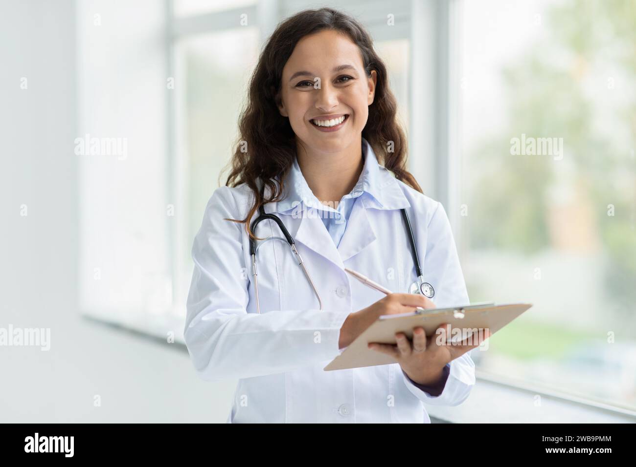 Positive young woman doctor taking notes in clipboard Stock Photo - Alamy