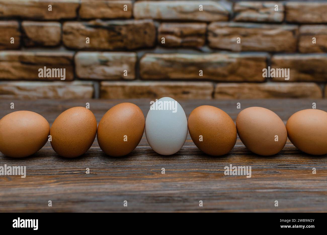 The photograph shows seven eggs arranged in a row on a wooden table in ...