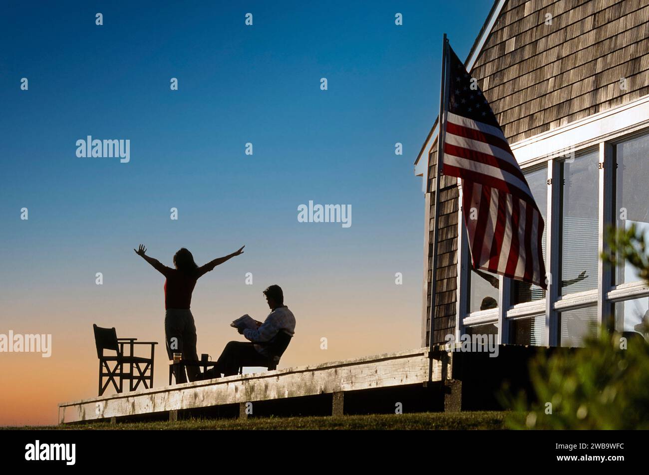 A wife stretches on the deck of there quetion home as a husband relaxes ...