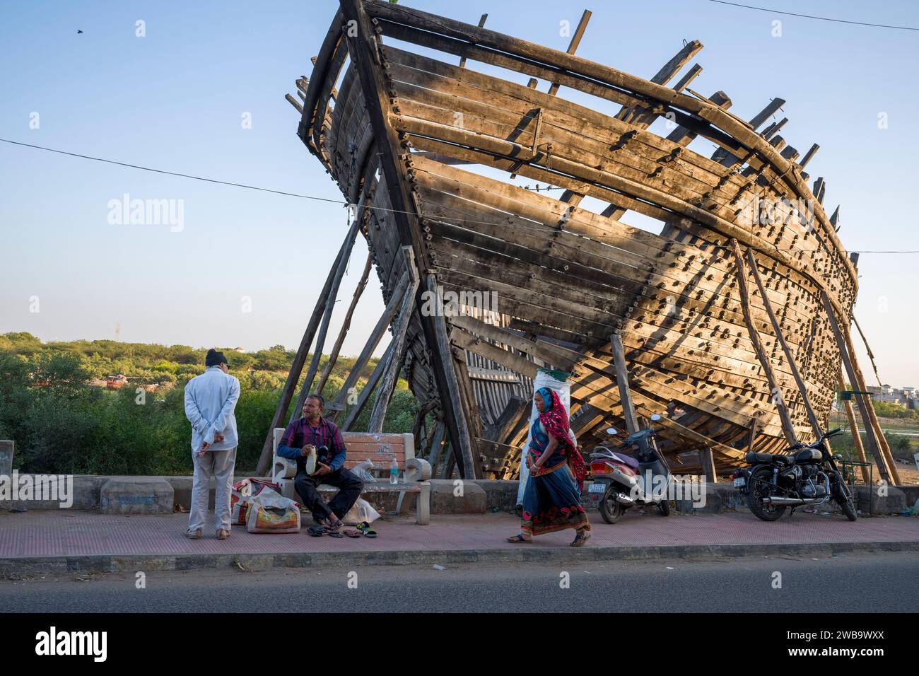 A street hawker sits on a public bench in front of the prow of a ...