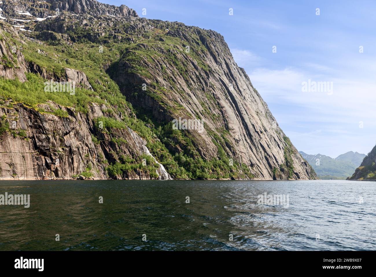 A small waterfall interrupts the steep, striated rock faces of ...