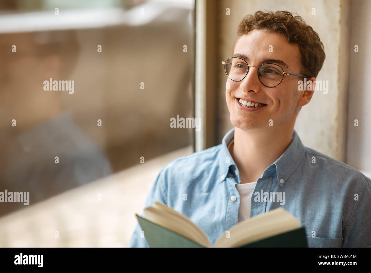 Glad calm handsome european young man student in glasses read book ...