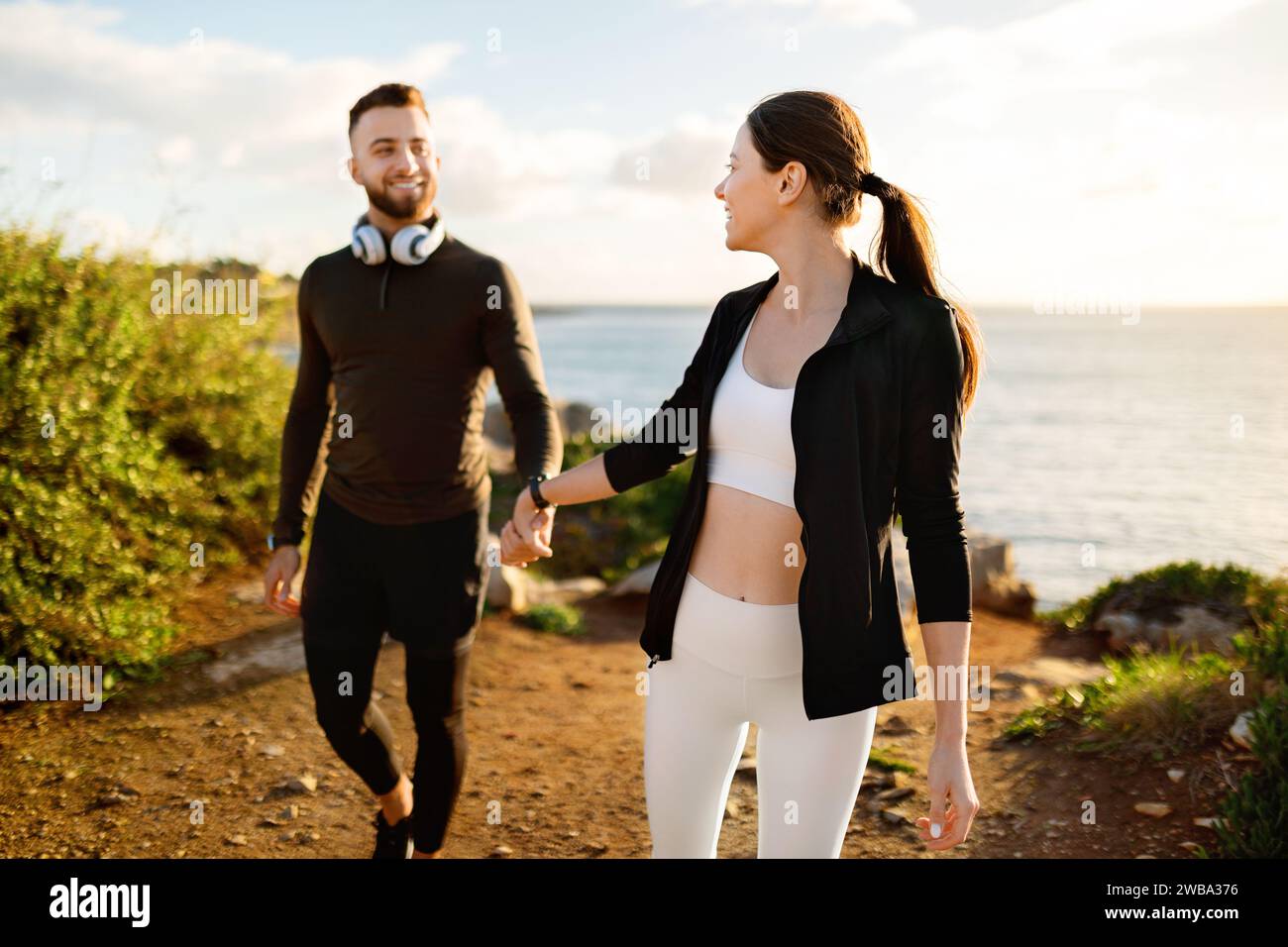 Couple holding hands and smiling on seaside walk after workout Stock ...