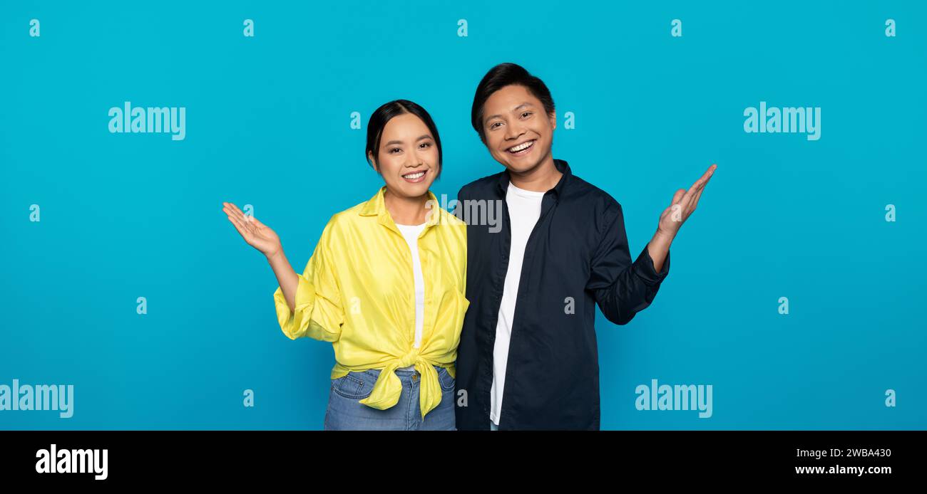 Smiling Asian man and woman standing with palms open in a welcoming ...