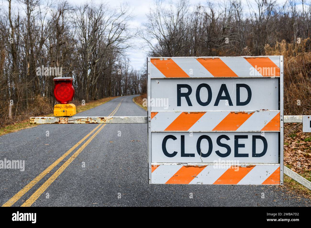 Road closed sign on a rust gate with a red flashing warning light with ...