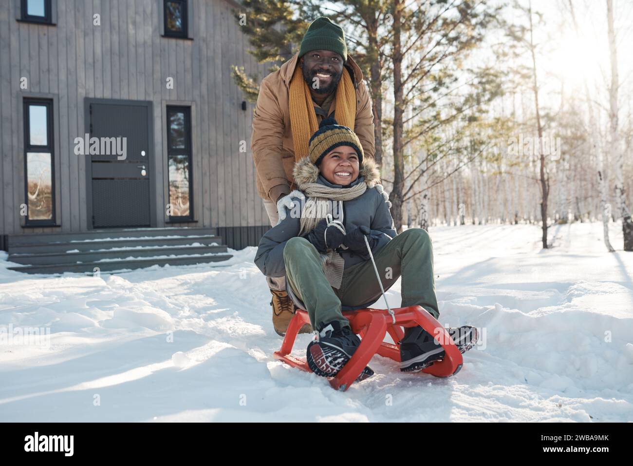 Happy young African American man in warm winterwear pushing sledge with ...