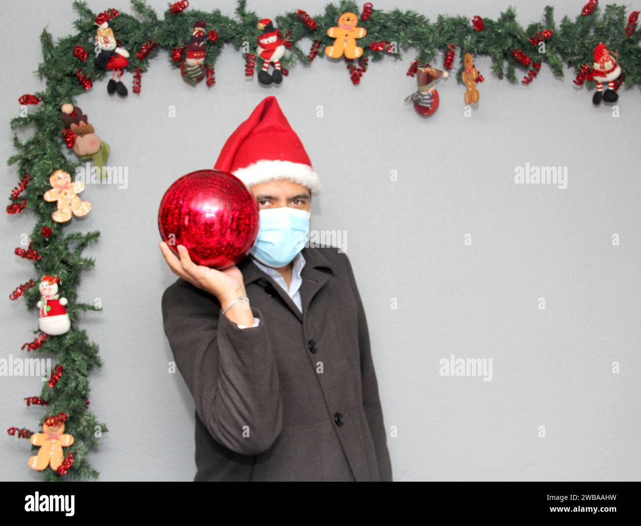 Latin man with protection mask, santa claus hat and red sphere ...