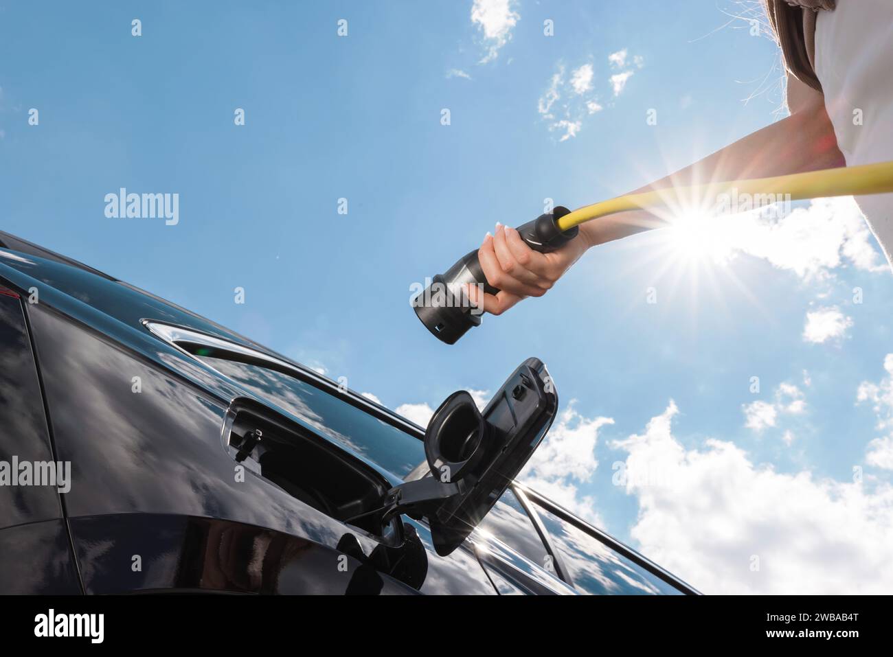 Woman opening an electric car charging socket cap and plugging in a ...