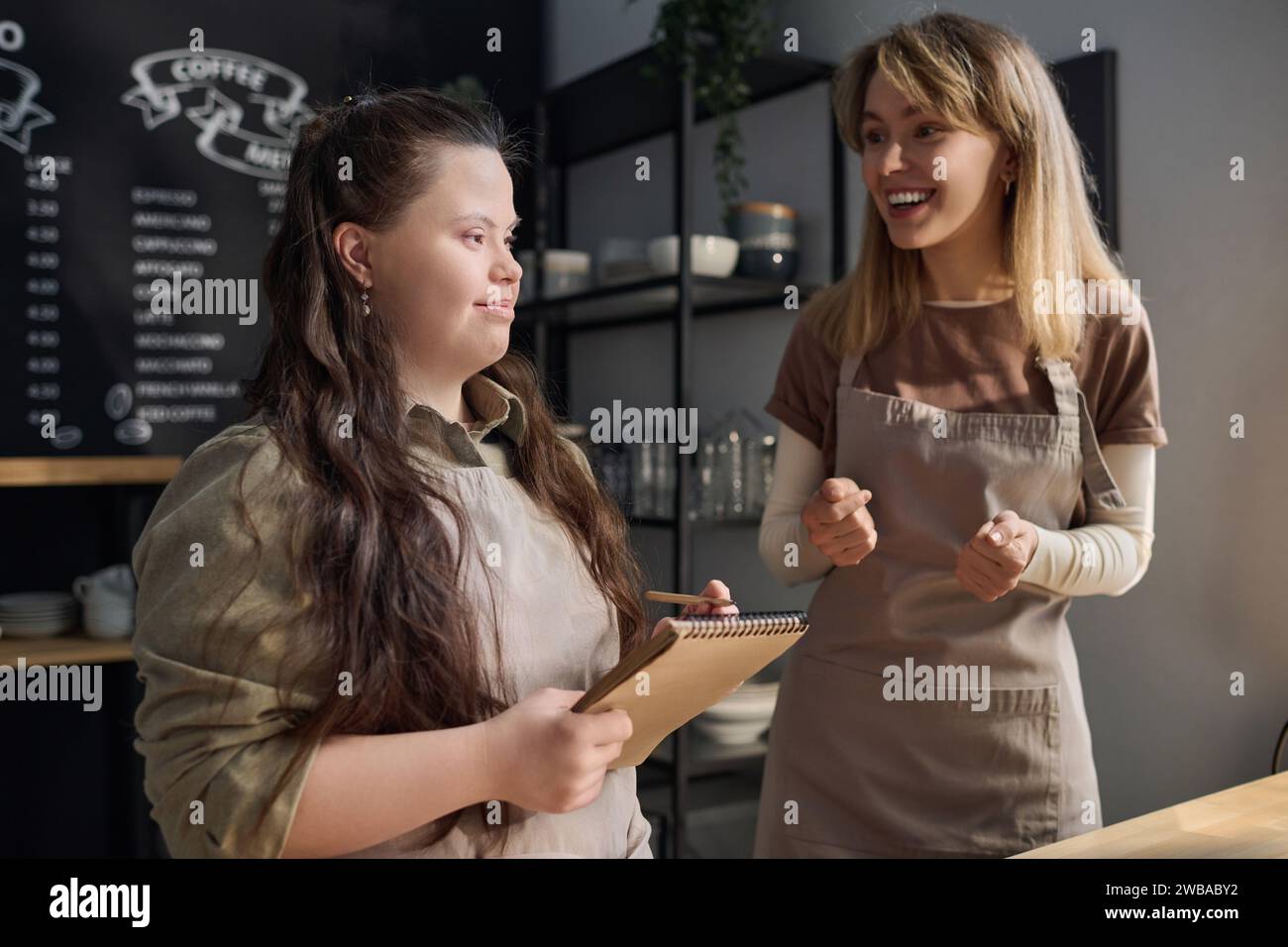 Happy young waitress looking at her female colleague with disability ...