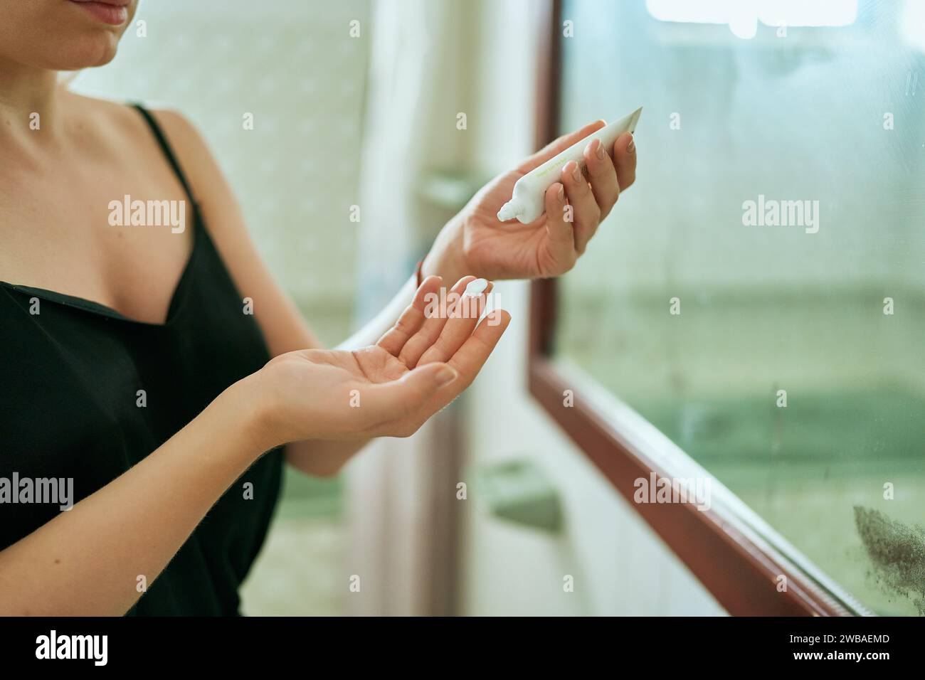 Woman applies moisturizer on hand in vintage bathroom setting. Personal ...