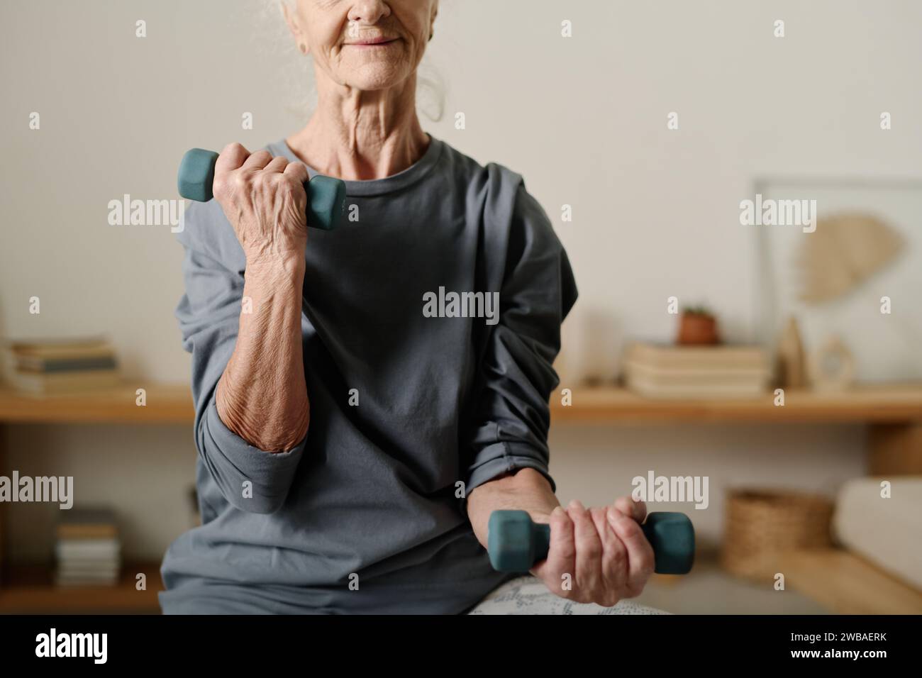 Active retired woman with dumbbells in hands pumping arm muscles during ...