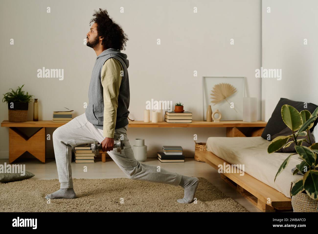 Side view of young sportsman with metallic dumbbells in hands keeping ...