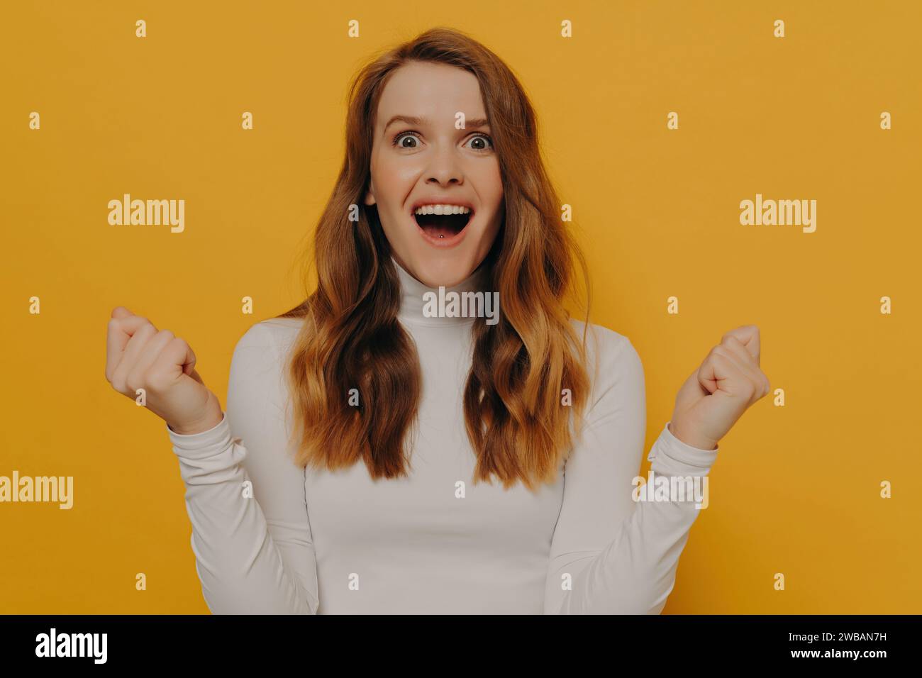 Ecstatic young woman with hands raised in victory, mouth open in a ...