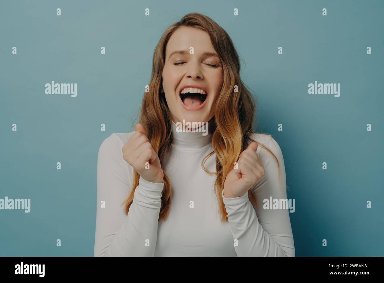 Exuberant young woman in white turtleneck laughing with eyes closed ...
