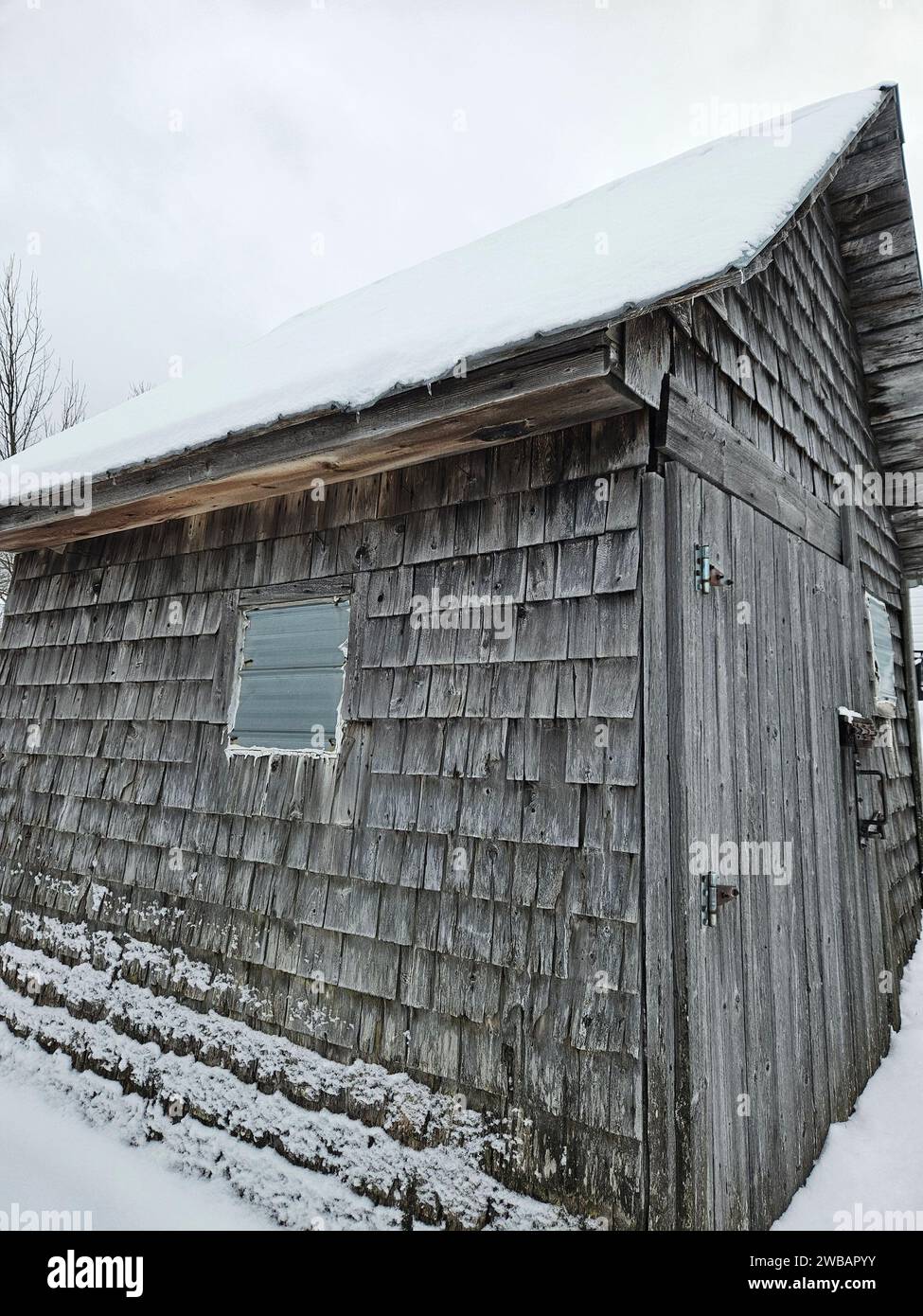 A rustic wooden shed with a coating of snow on its roof, giving the ...