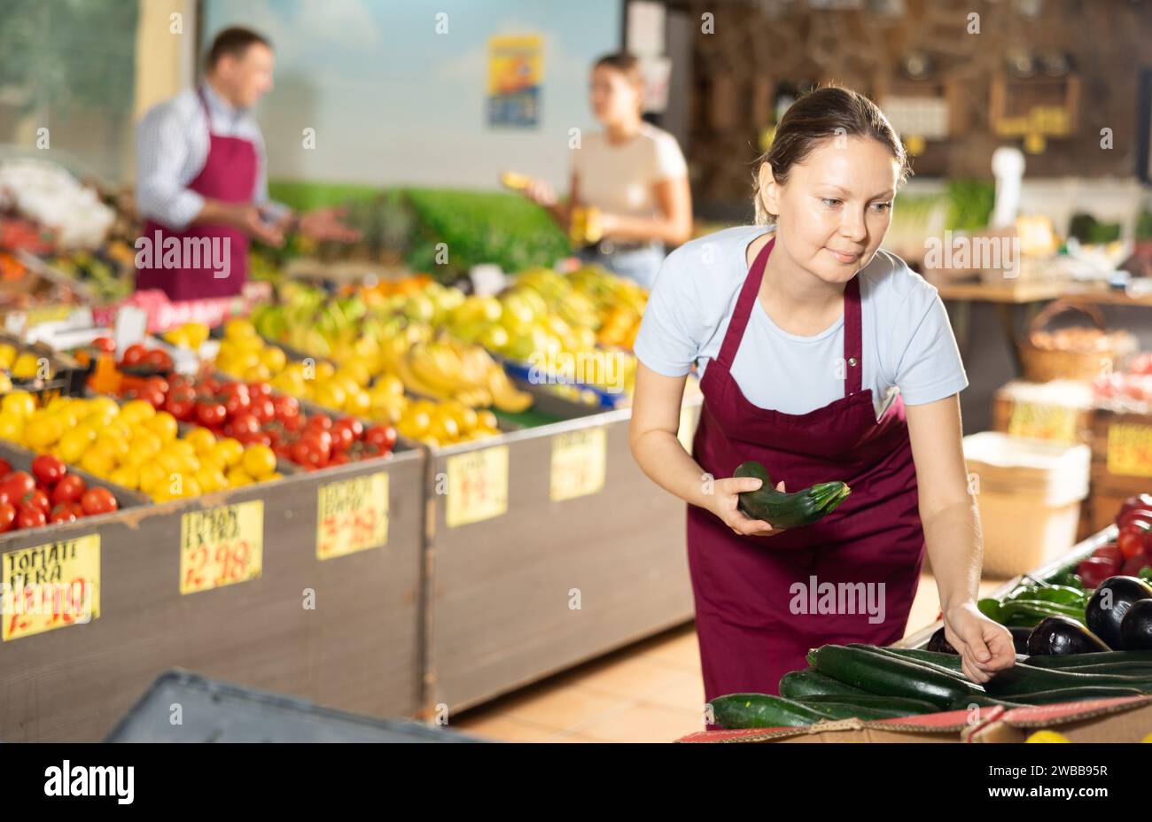 Woman seller of fruit and vegetable store works near showcase with ...
