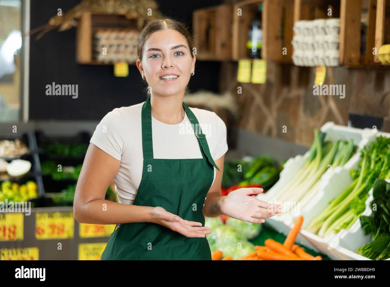 Female seller in uniform standing among shelves with fruits and ...