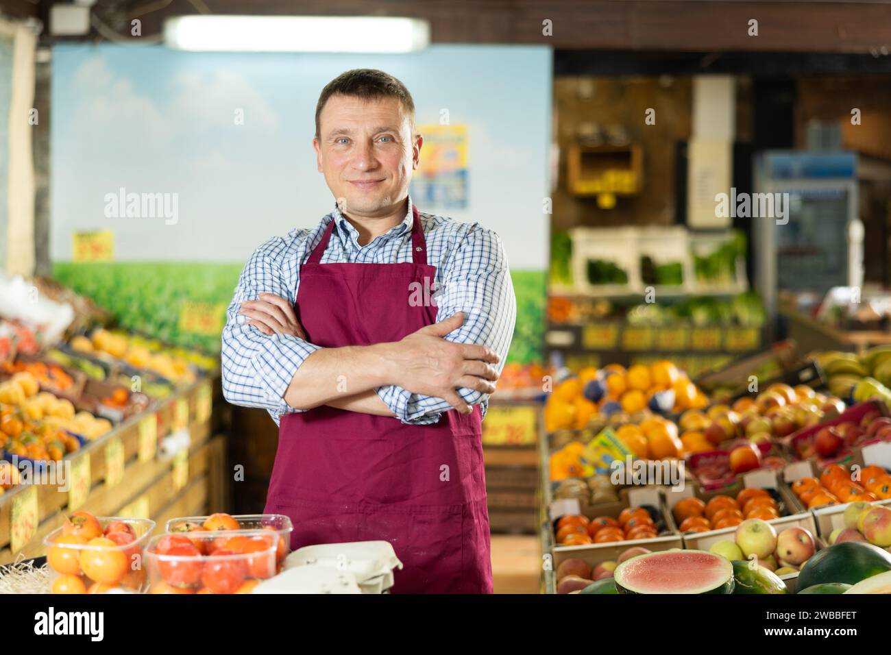 Positive and friendly store man employee stands with arms crossed on ...
