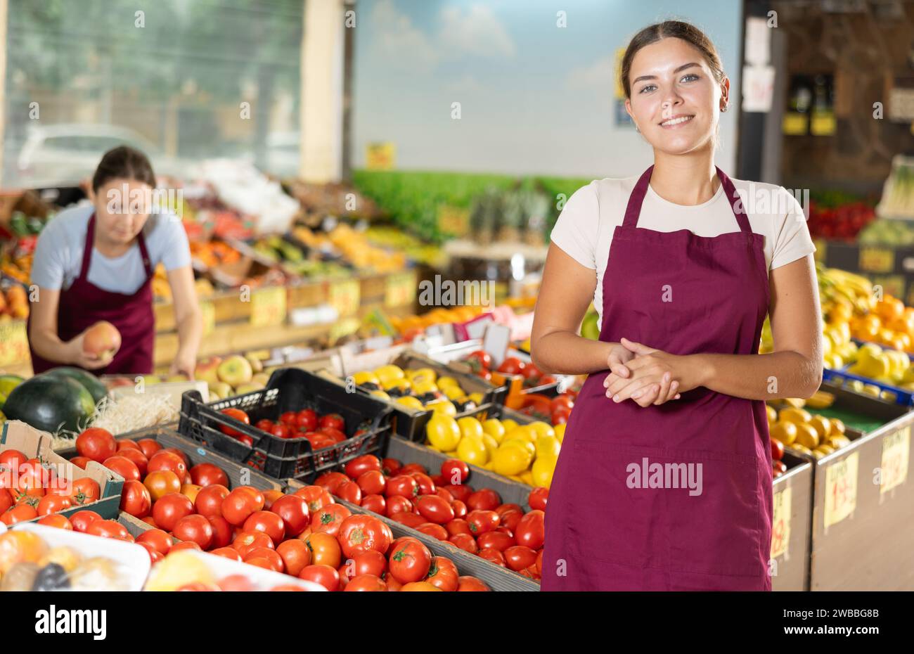 Positive and friendly store girl employee stands with arms crossed on chest and waits for ...
