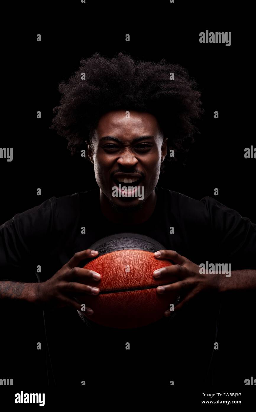 Basketball player holding a ball against black background and screaming ...